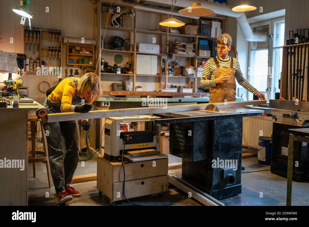 Family carpenters use table saw to cut wooden beams in workshop. Hands ...
