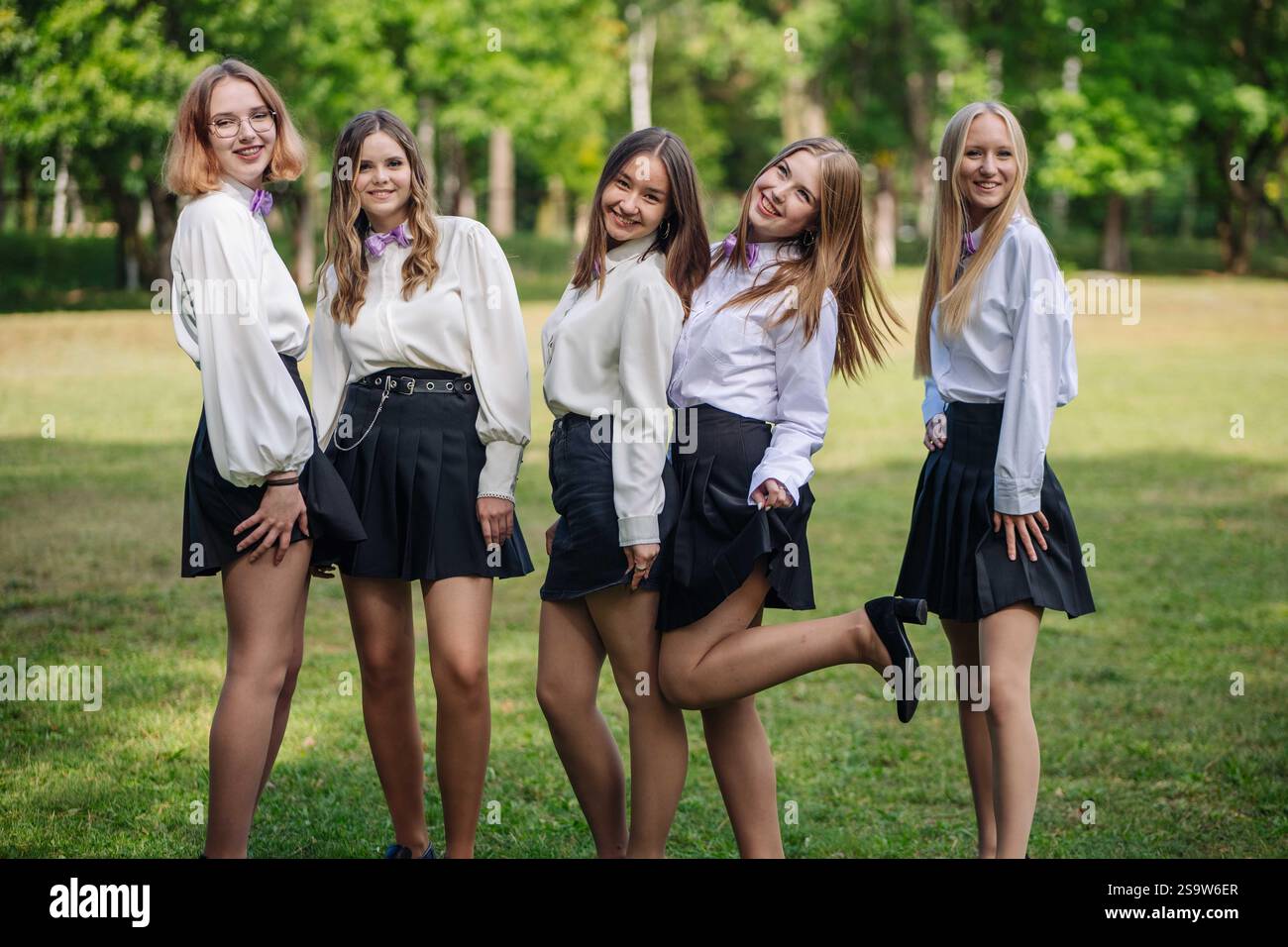 Five jubilant schoolgirls in uniform posing together in a park on their ...