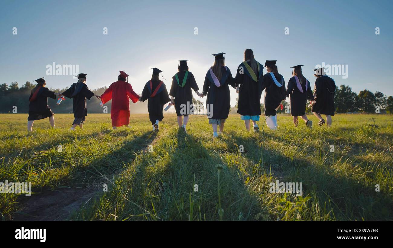 Students in graduation attire walking through a sunset drenched field ...
