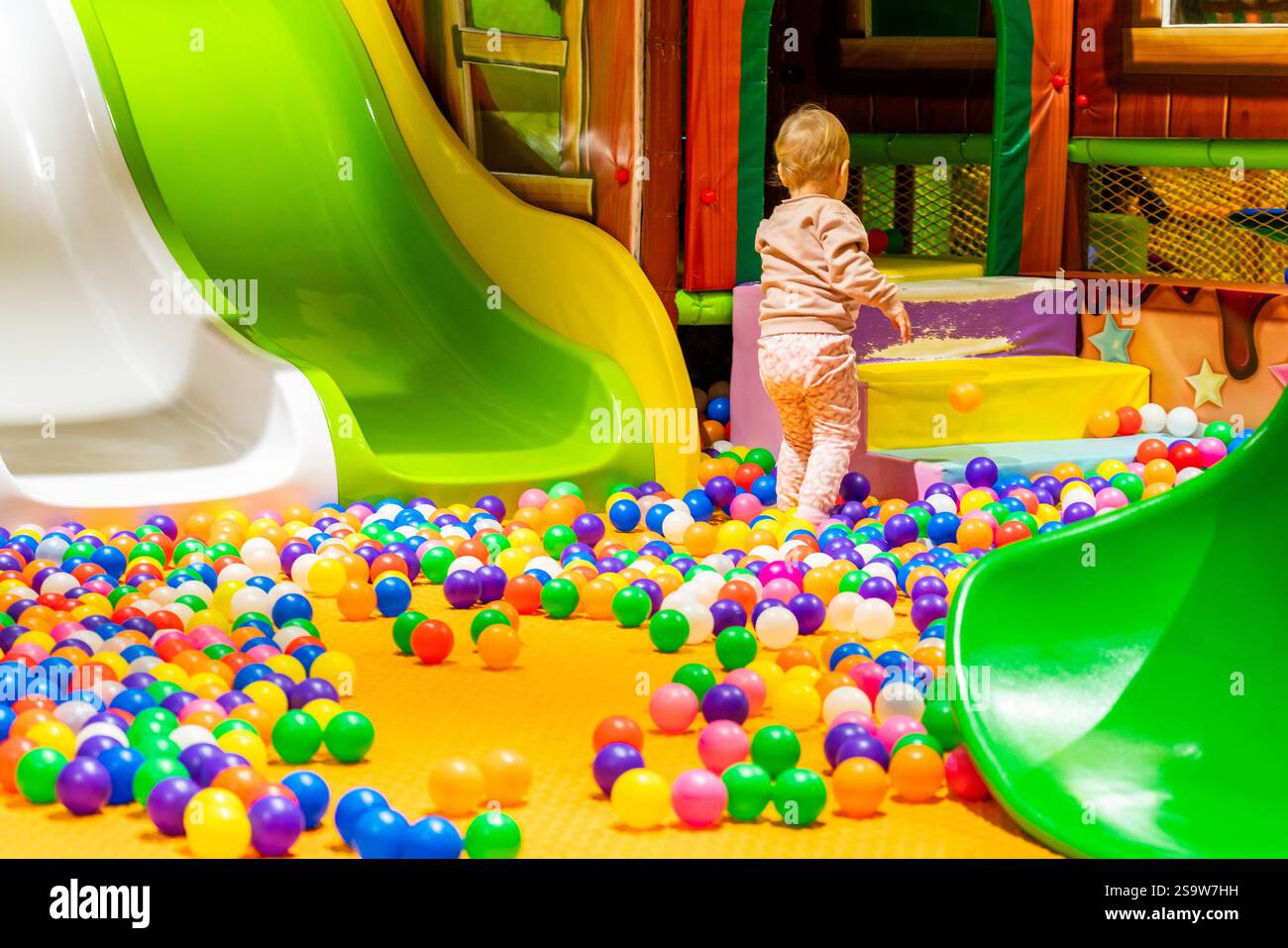 A joyful toddler exploring a colorful indoor playground with slides and ...
