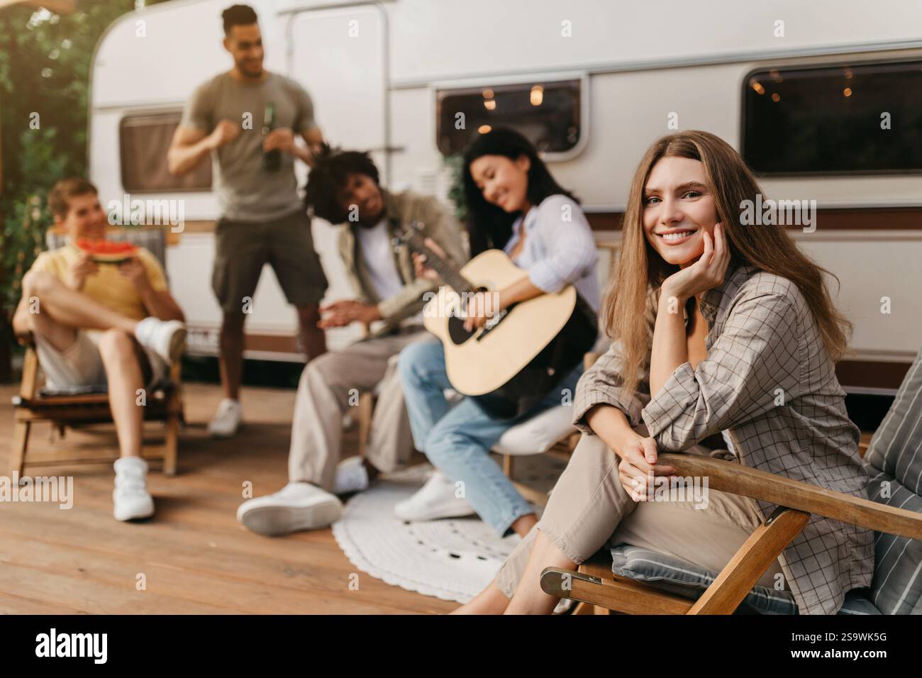 Cool young people having fun on camping trip, sitting in lounge chairs ...