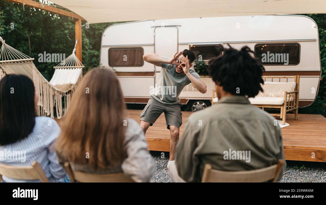 Multiracial young friends playing charades near motorhome during ...