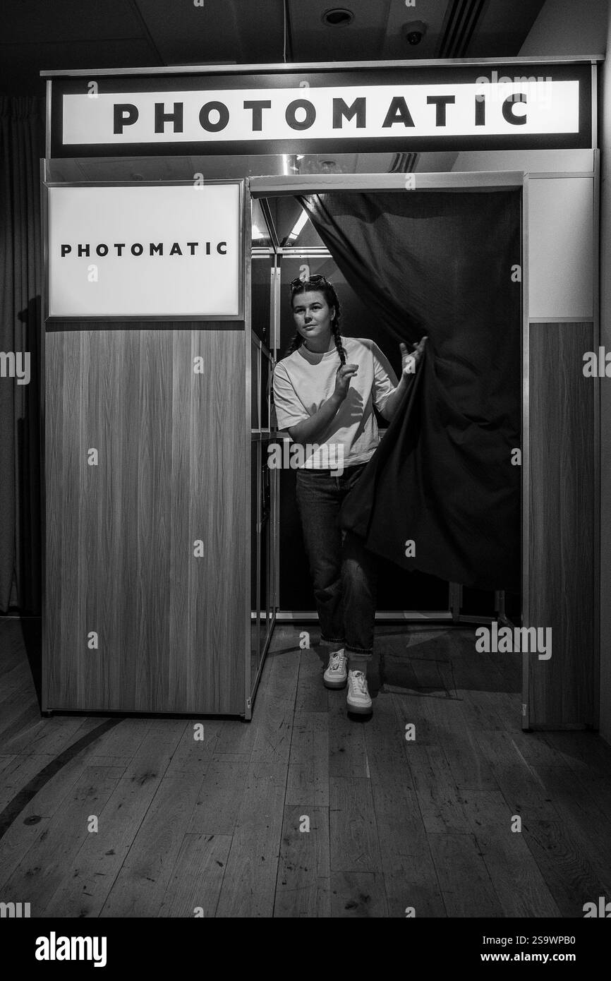 Young lady exiting Photo booth, pulling back the cloth. Black-and-white ...