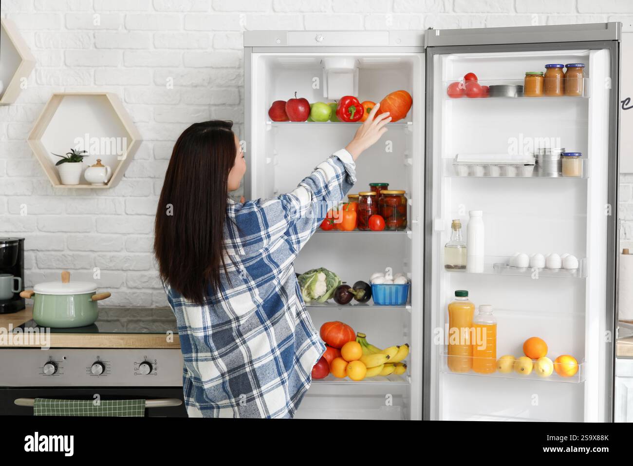 Young woman taking fresh food from open fridge in kitchen, back view ...