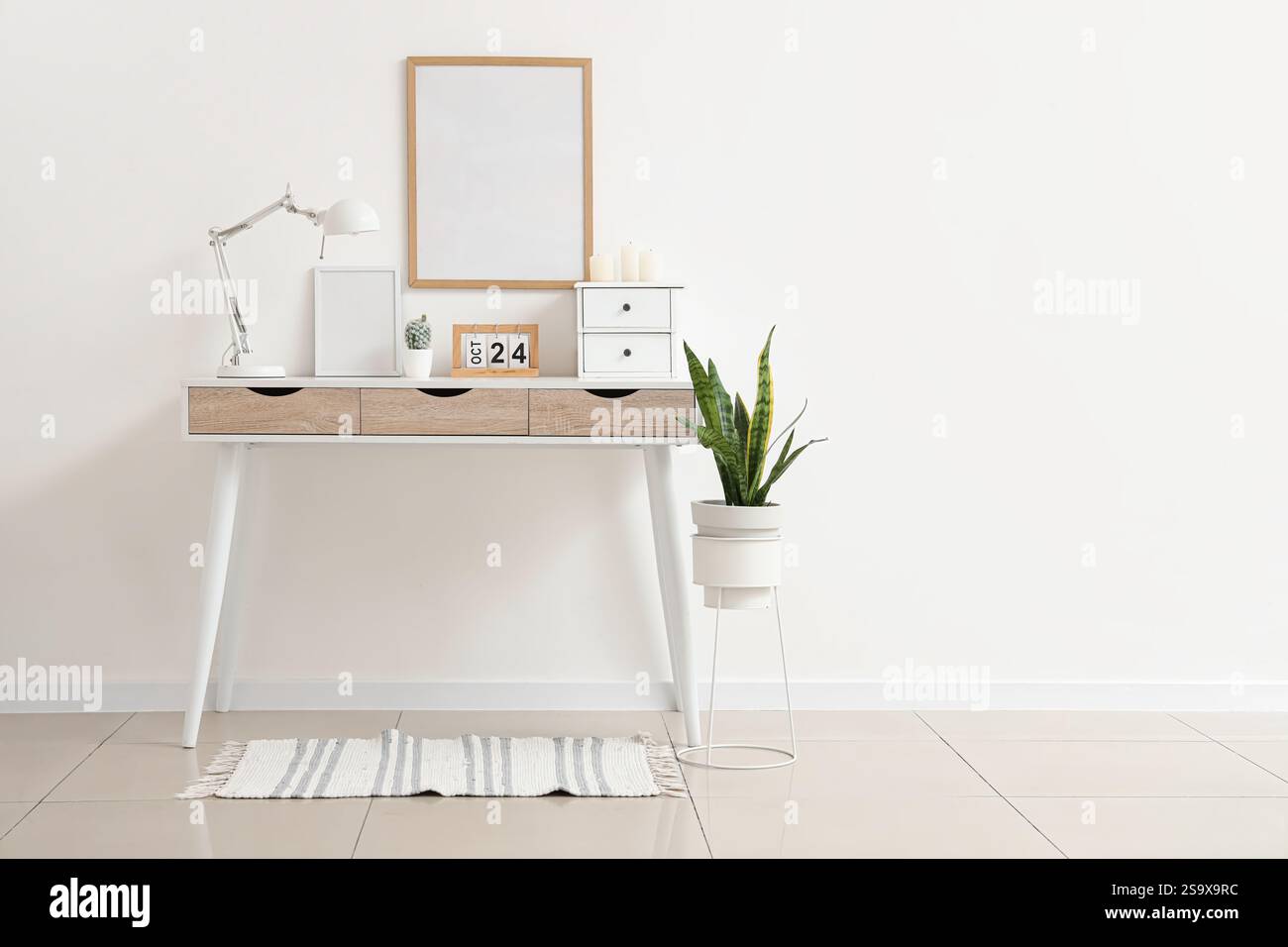 Modern table with stylish desk lamp, calendar and candles near white ...