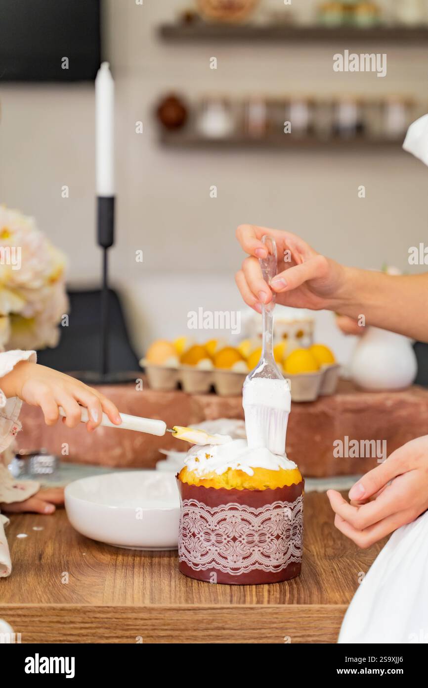 Mom and child together apply cream to Easter cake with brushes. Easter ...