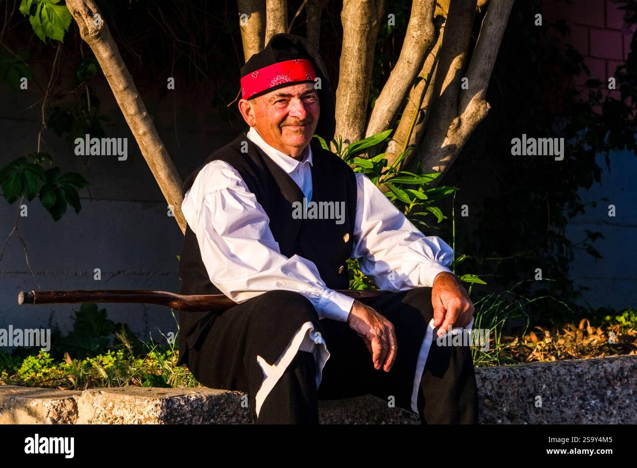 Portrait of a traditionally dressed old man, resting on a wall, taking ...