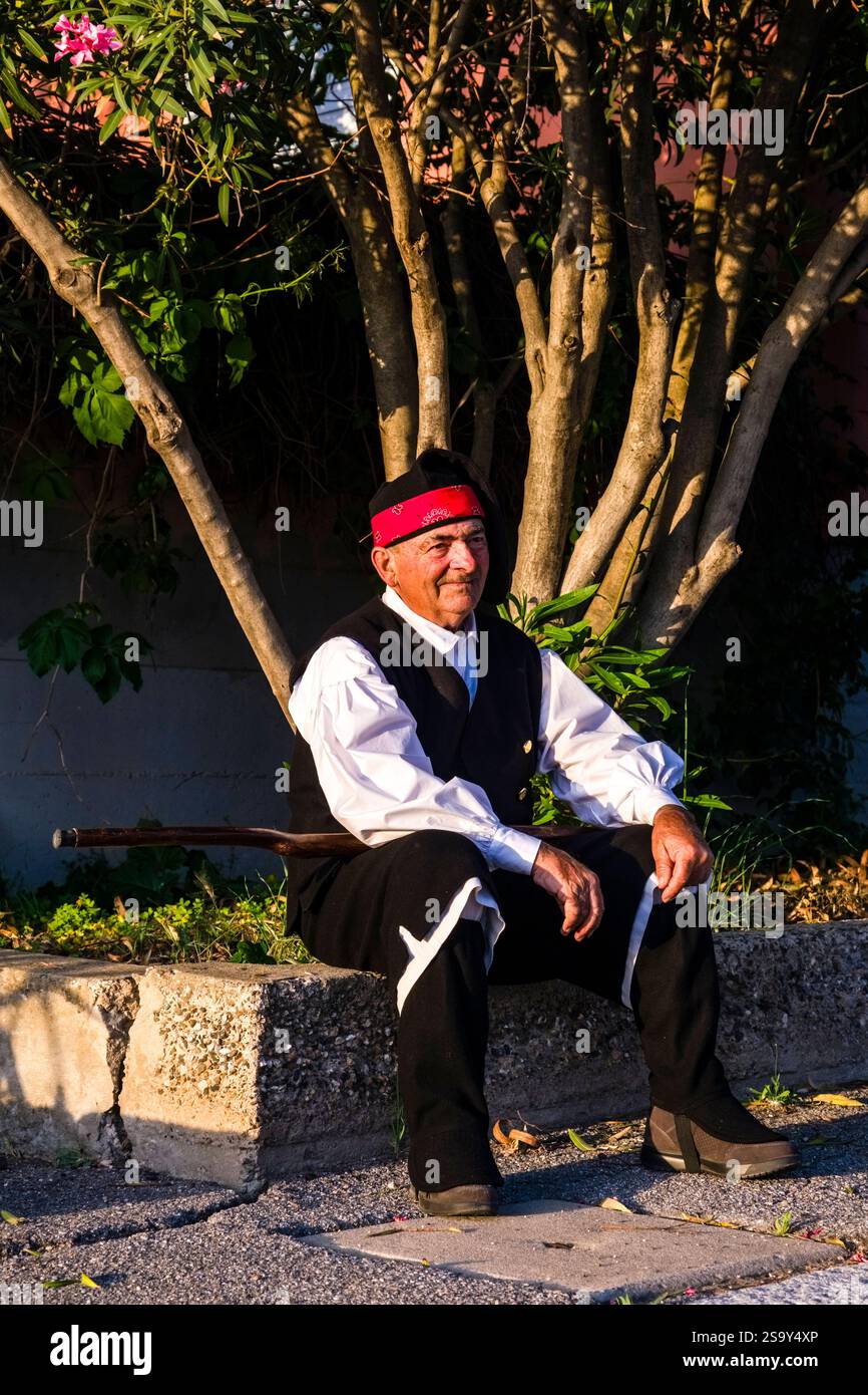 Portrait of a traditionally dressed old man, resting on a wall, taking ...