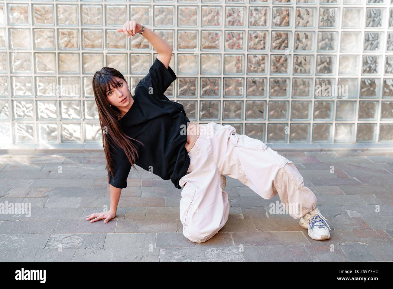 Young dancer performs dynamic moves against a glass block wall in urban ...