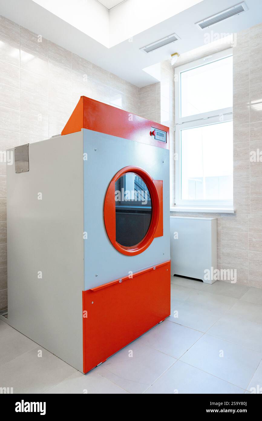 Modern laundry room featuring a large industrial washer with orange and ...