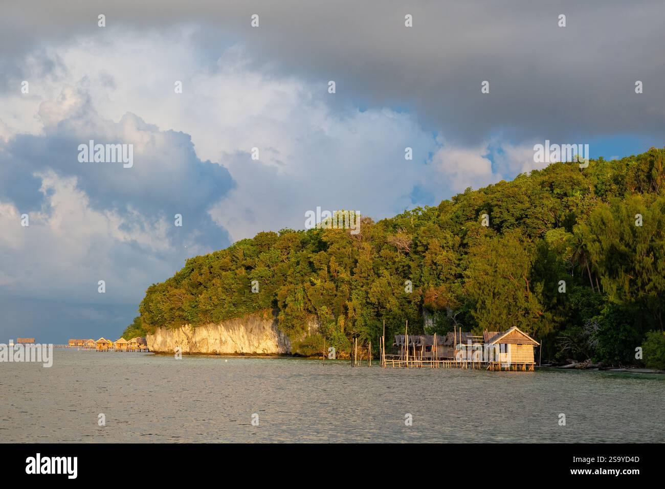 A stilted hut sits by a lush green coastline, with towering trees and a ...