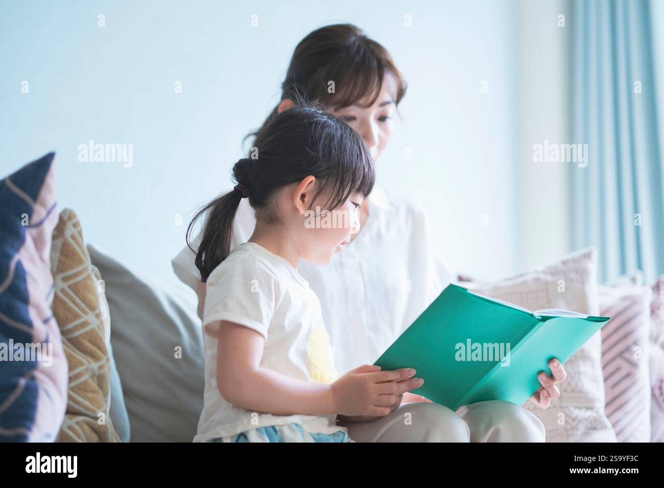Parent and child reading a picture book on a sofa Stock Photo - Alamy