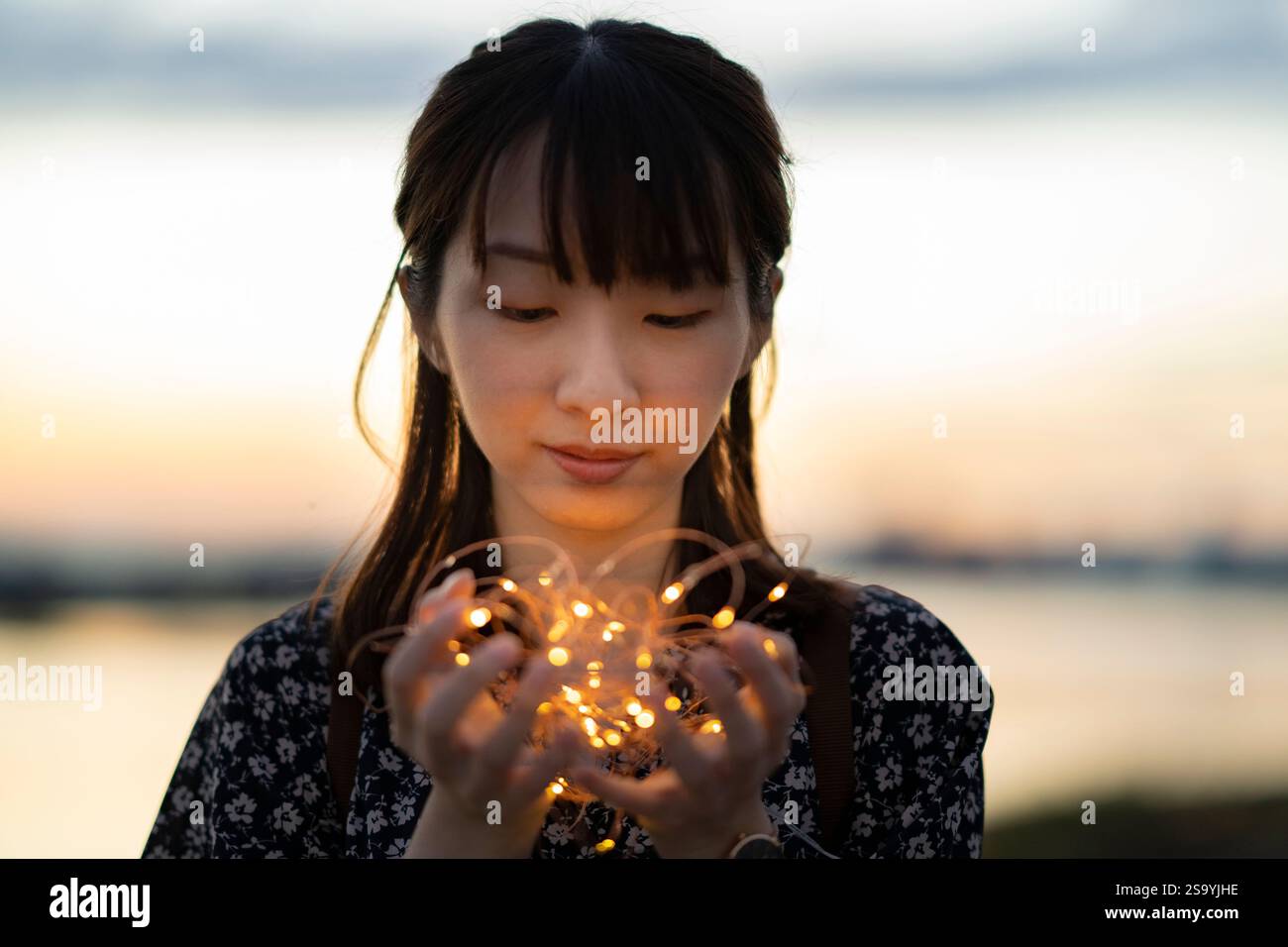 Young woman wrapping her hands around an illuminated light Stock Photo ...