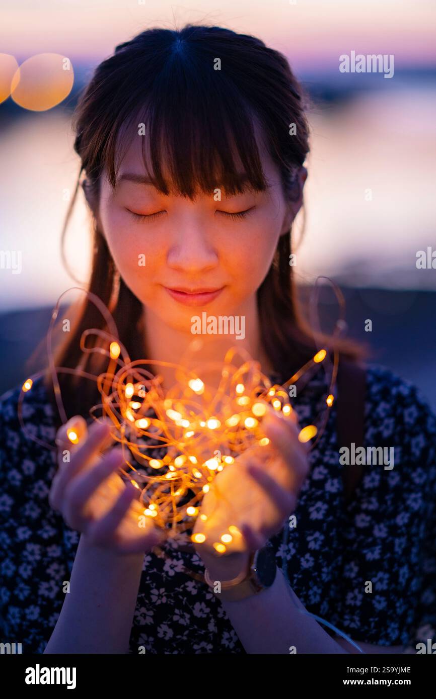 Young woman wrapping her hands around an illuminated light Stock Photo ...