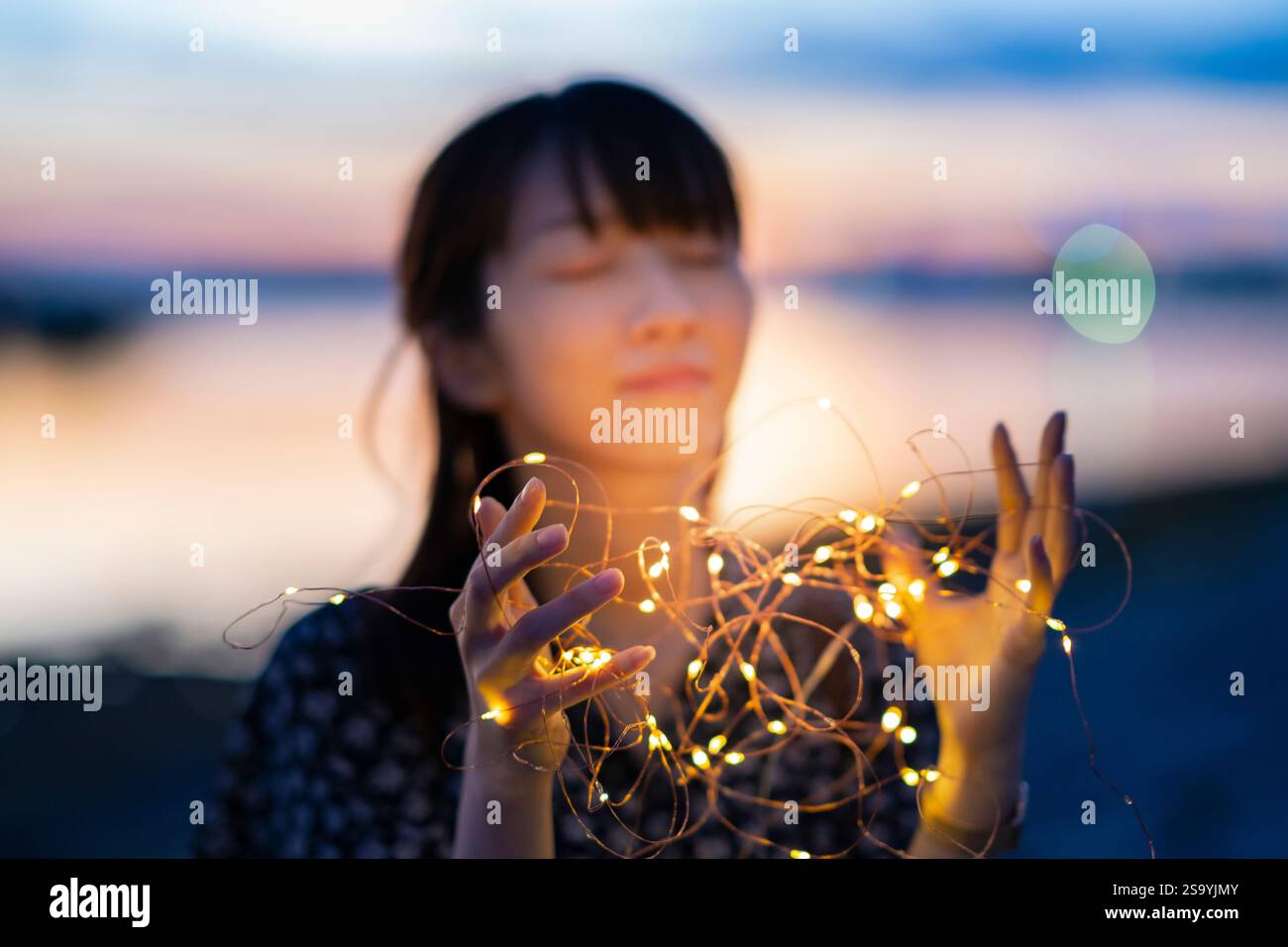Young woman wrapping her hands around an illuminated light Stock Photo ...