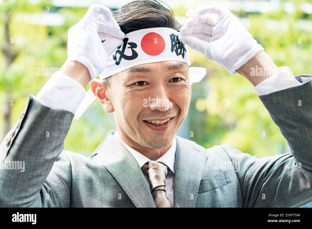 A man in a suit wearing a ‘must-win’ hachimaki on his head Stock Photo ...