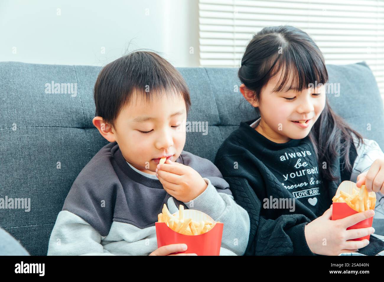 Children sitting on a sofa and eating a snack Stock Photo - Alamy