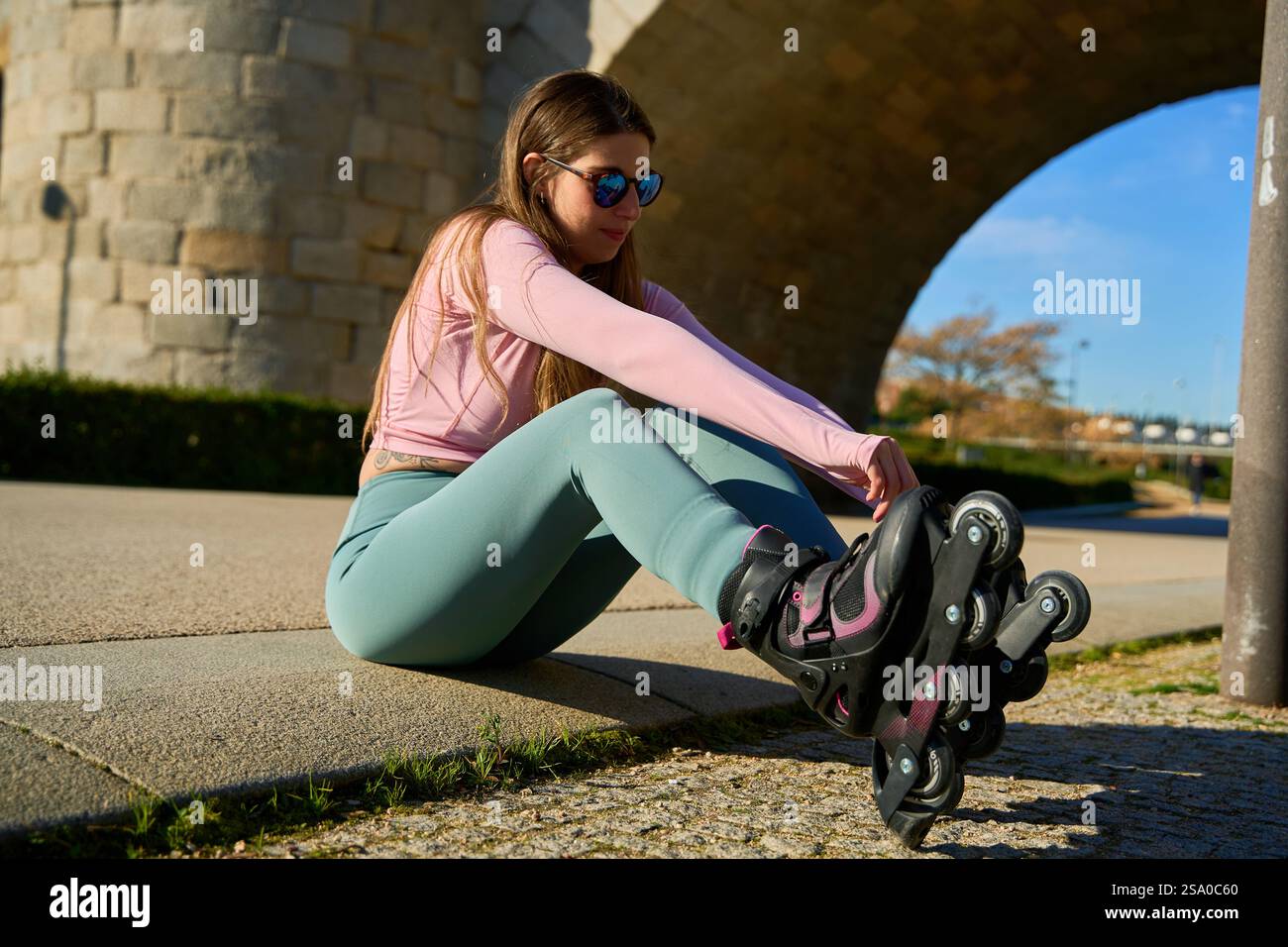 Sporty woman tying her inline skates sitting on the ground, ready for ...