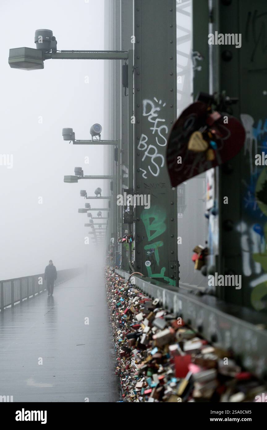 A person walks along a foggy bridge adorned with colorful love locks ...
