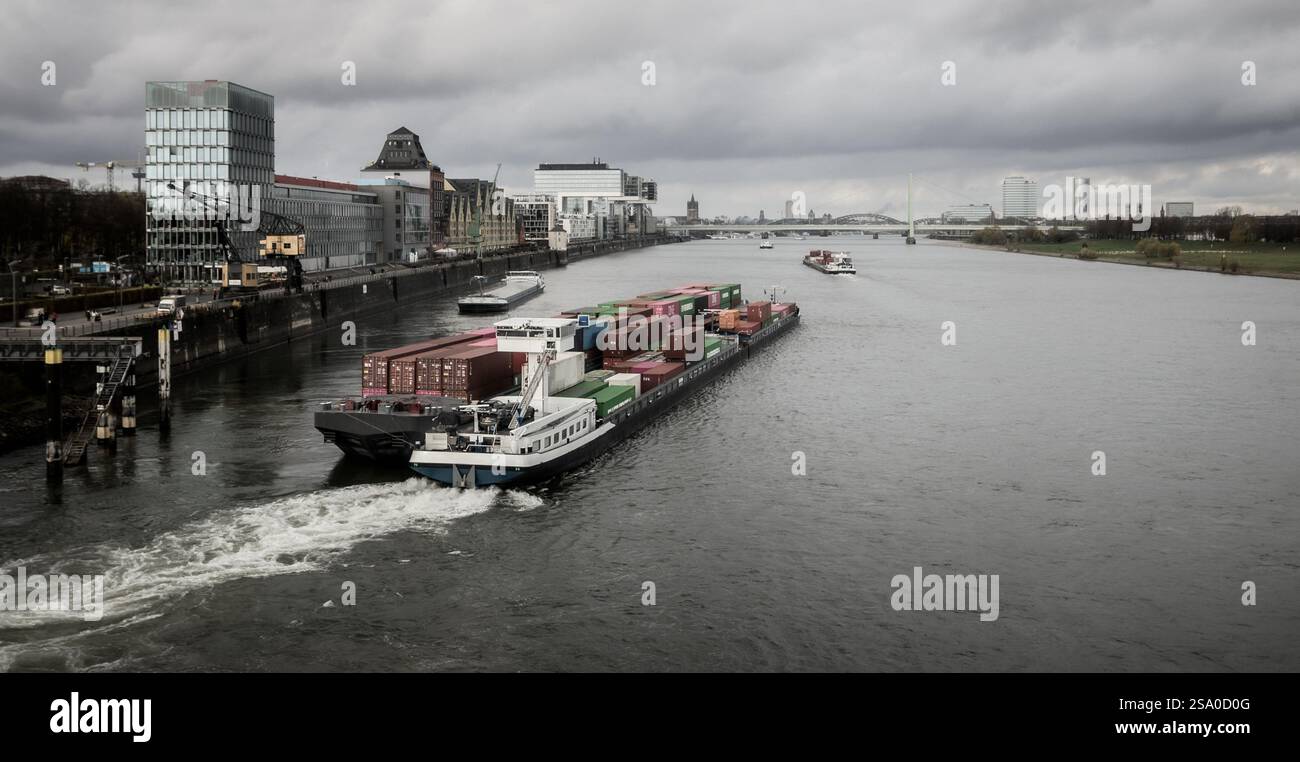 A cargo ship transports containers along a river, flanked by modern ...