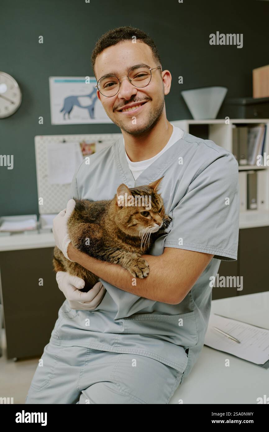 Veterinarian wearing glasses smiling while holding a cat in veterinary ...
