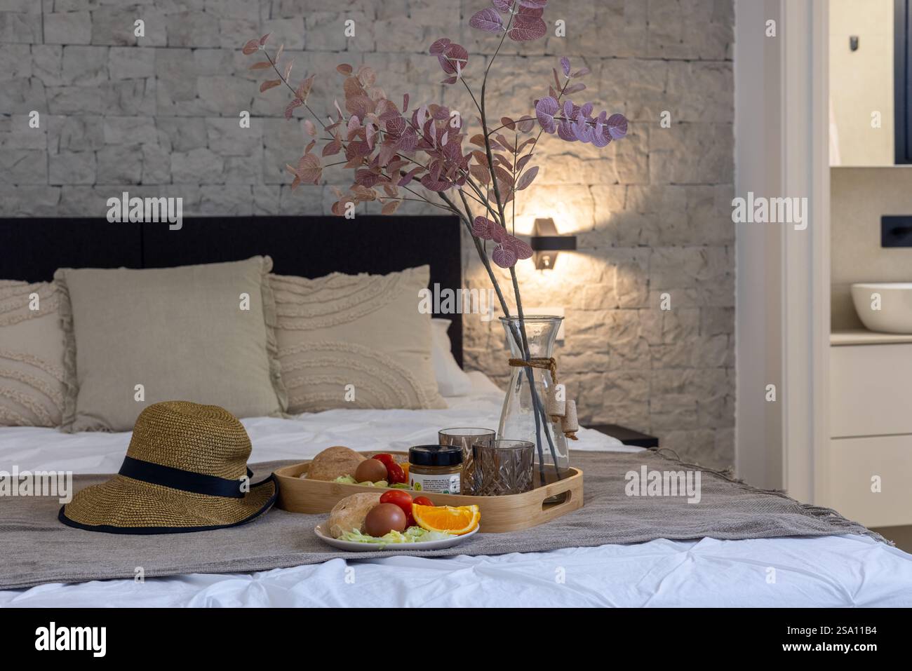 A cozy bed setup featuring a breakfast tray with food, a straw hat ...