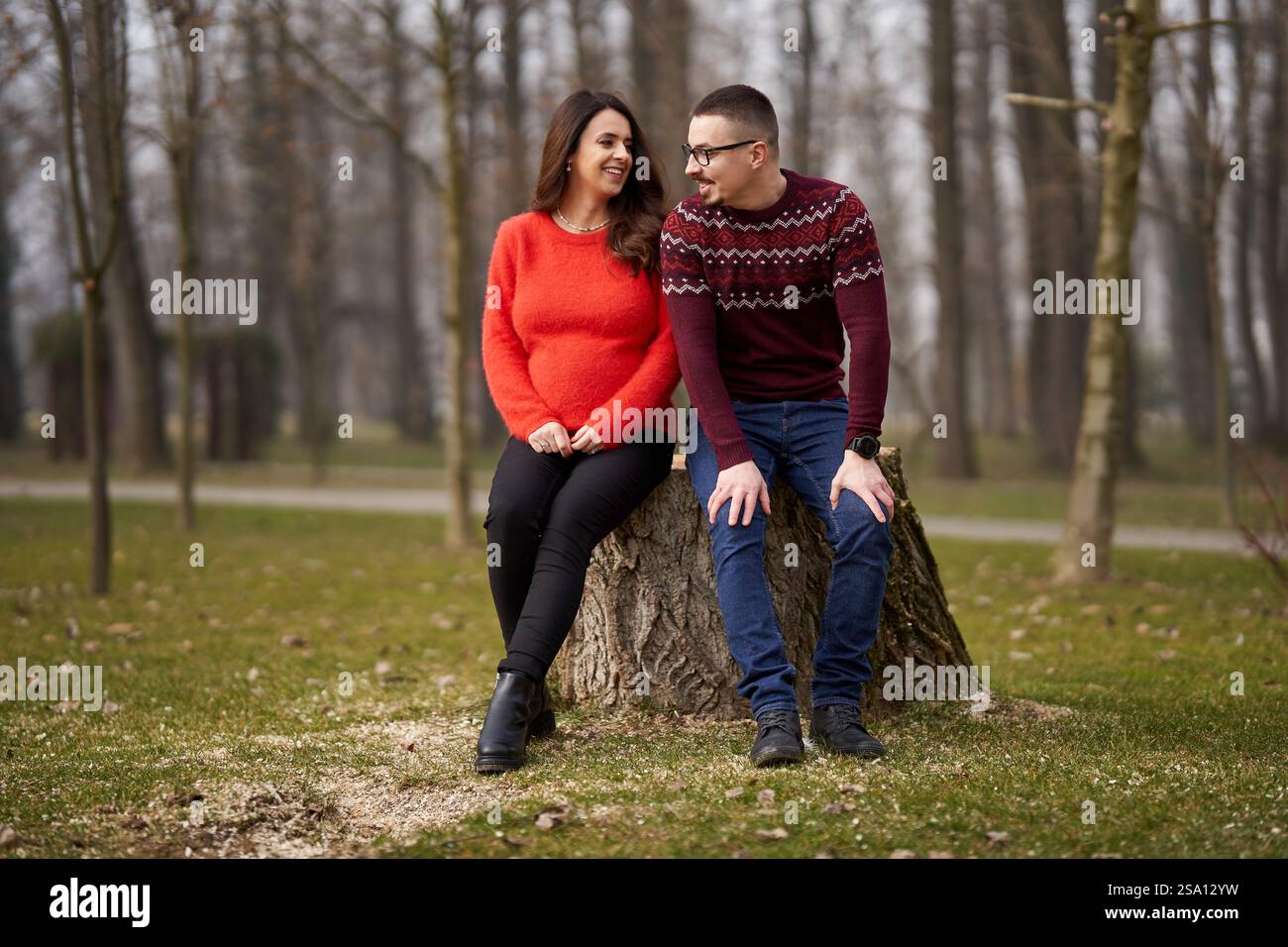 Happy expecting couple sitting on a tree stump in a park, embracing and ...