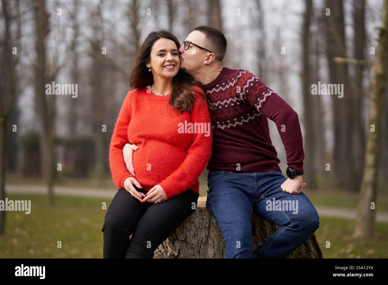 Happy expecting couple sitting on a tree stump in a park, embracing and ...