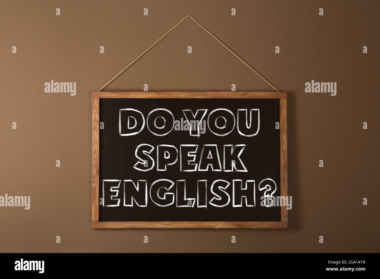 Small black chalkboard with text Do You Speak English? on brown wall ...