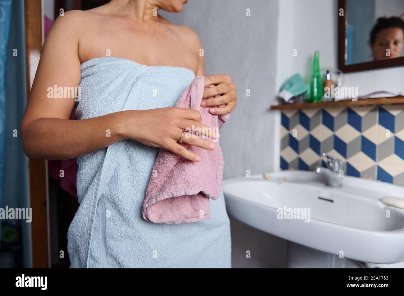 A woman wrapped in a towel holding a pink washcloth in a well-lit ...