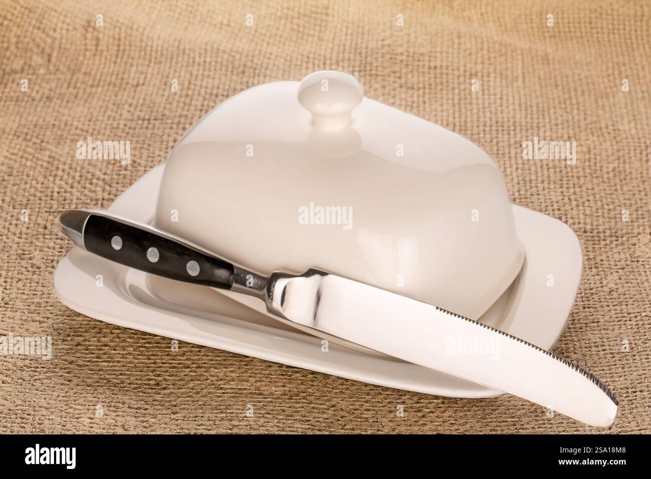 One ceramic butter container with a metal knife, macro, on jute cloth ...