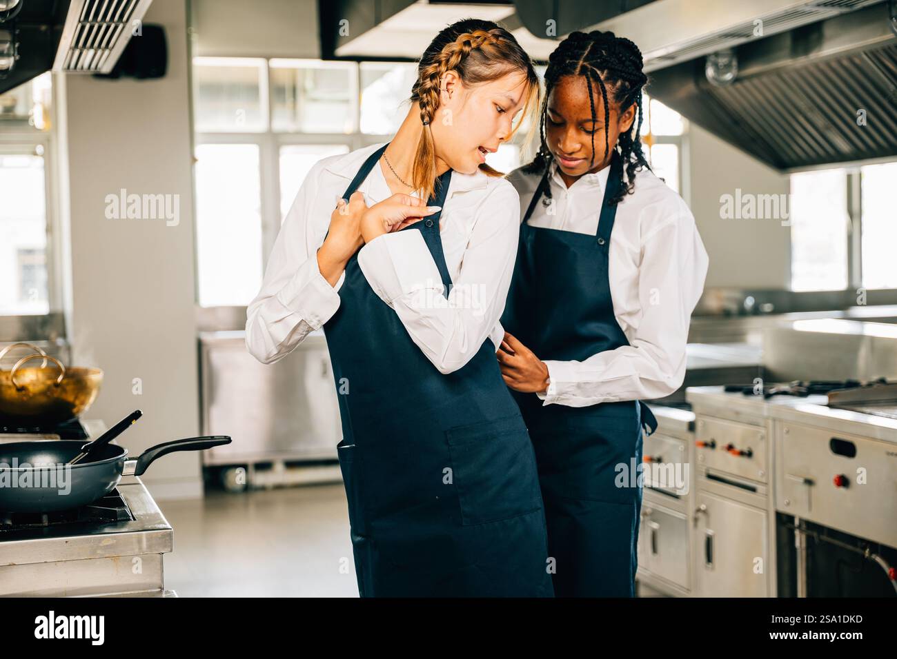 Girlfriend chef helps woman friend tie apron in a restaurant kitchen ...