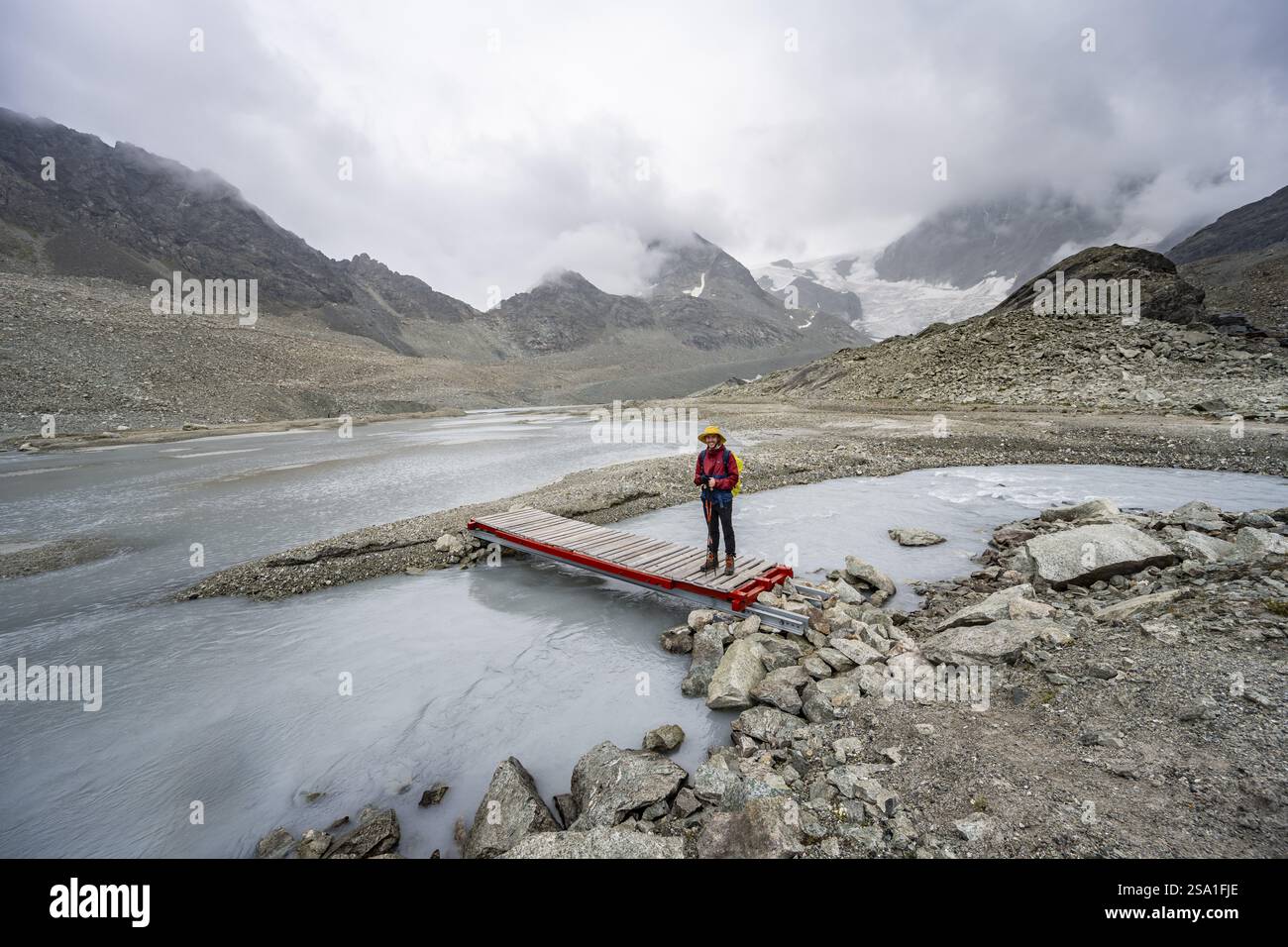 Mountaineer on a bridge over a glacial river of the glacier Glacier de ...