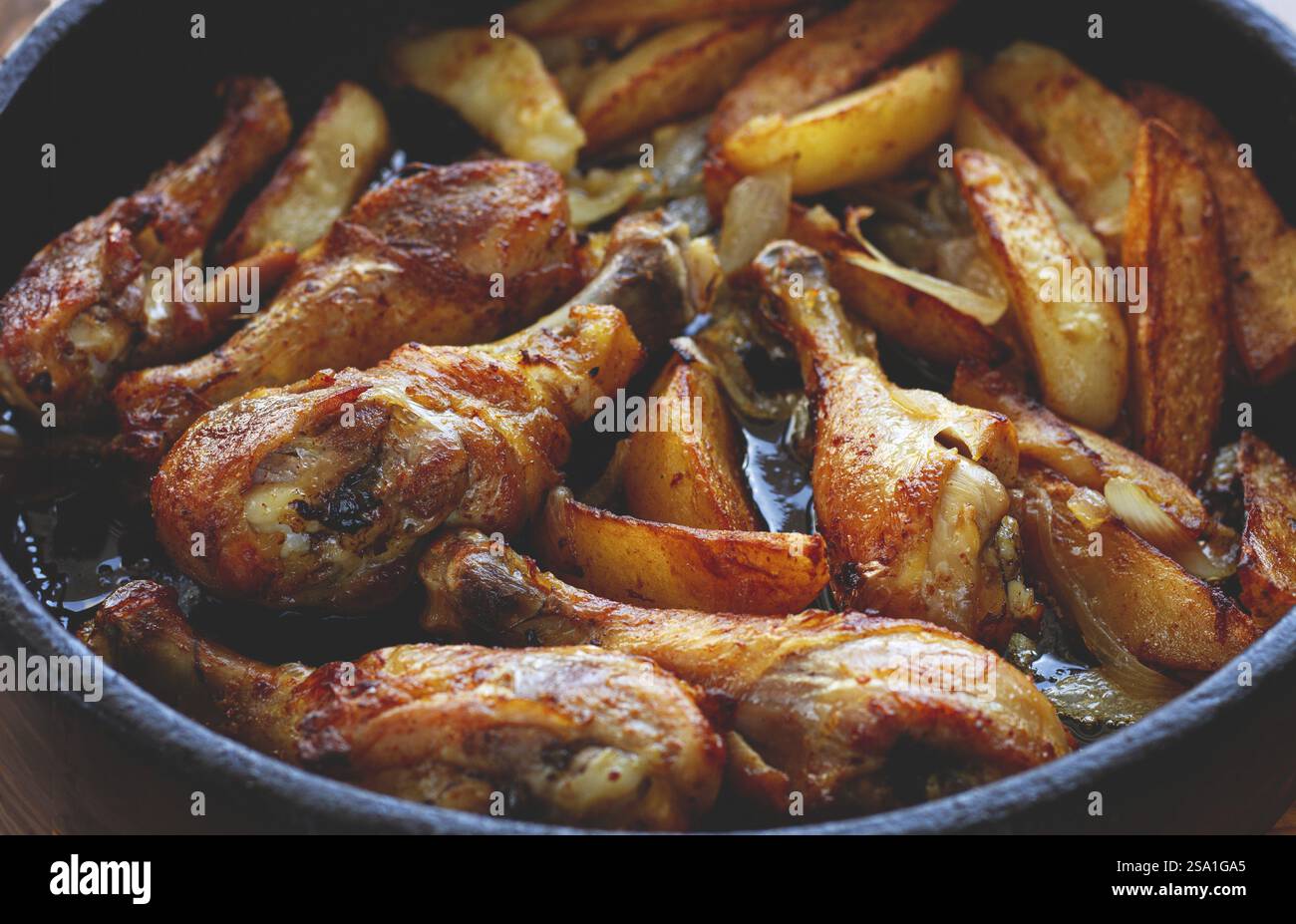 Fried chicken drumsticks with potato slices, in a clay pan, baked in ...