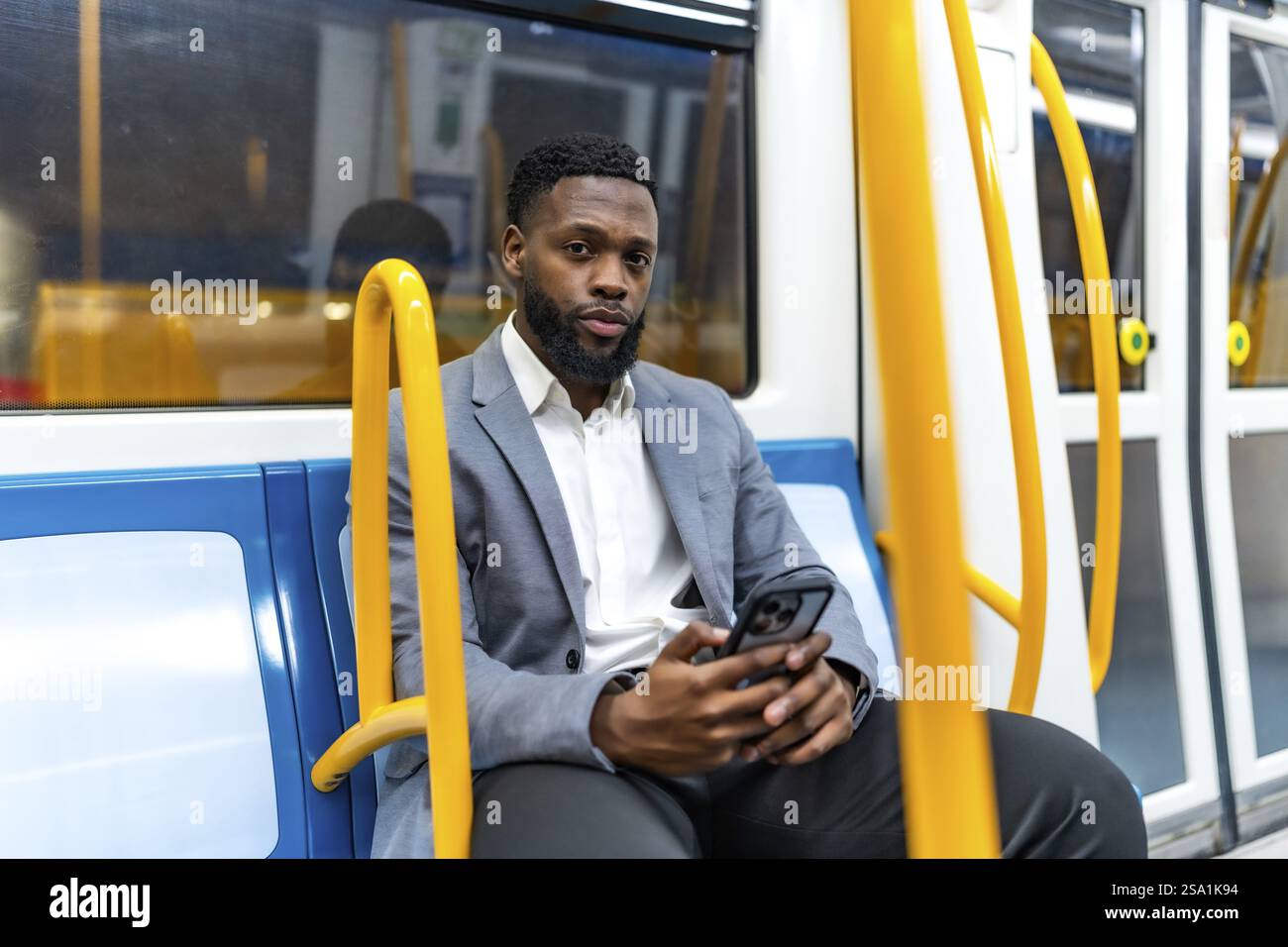 Young businessman sitting on a subway train, using a smartphone during ...
