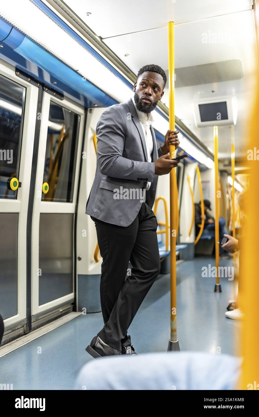 Young businessman holding handrail and using smartphone on subway train ...