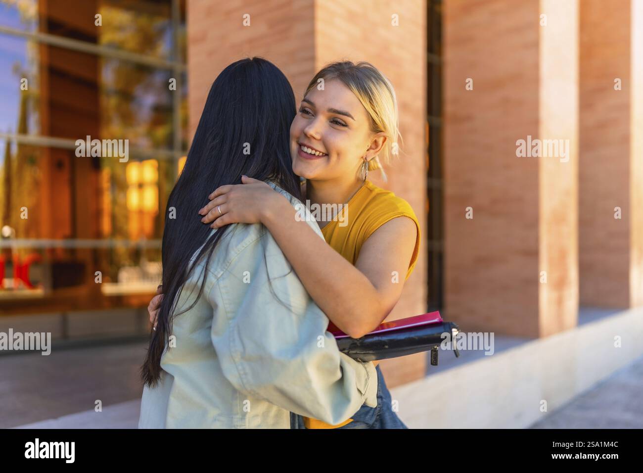 Student greeting a university mate and embracing her at the campus ...
