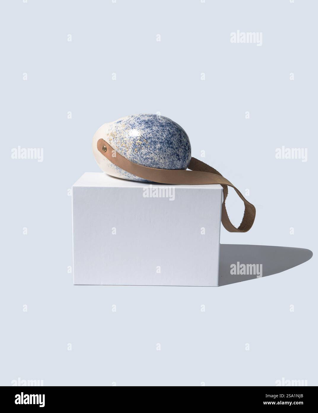 Textured rock with leather strap on white cube against light background Stock Photo - Alamy