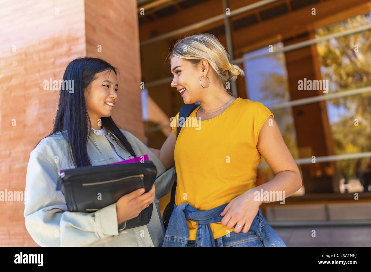 Happy female multi-ethnic university students talking outside the university building Stock ...