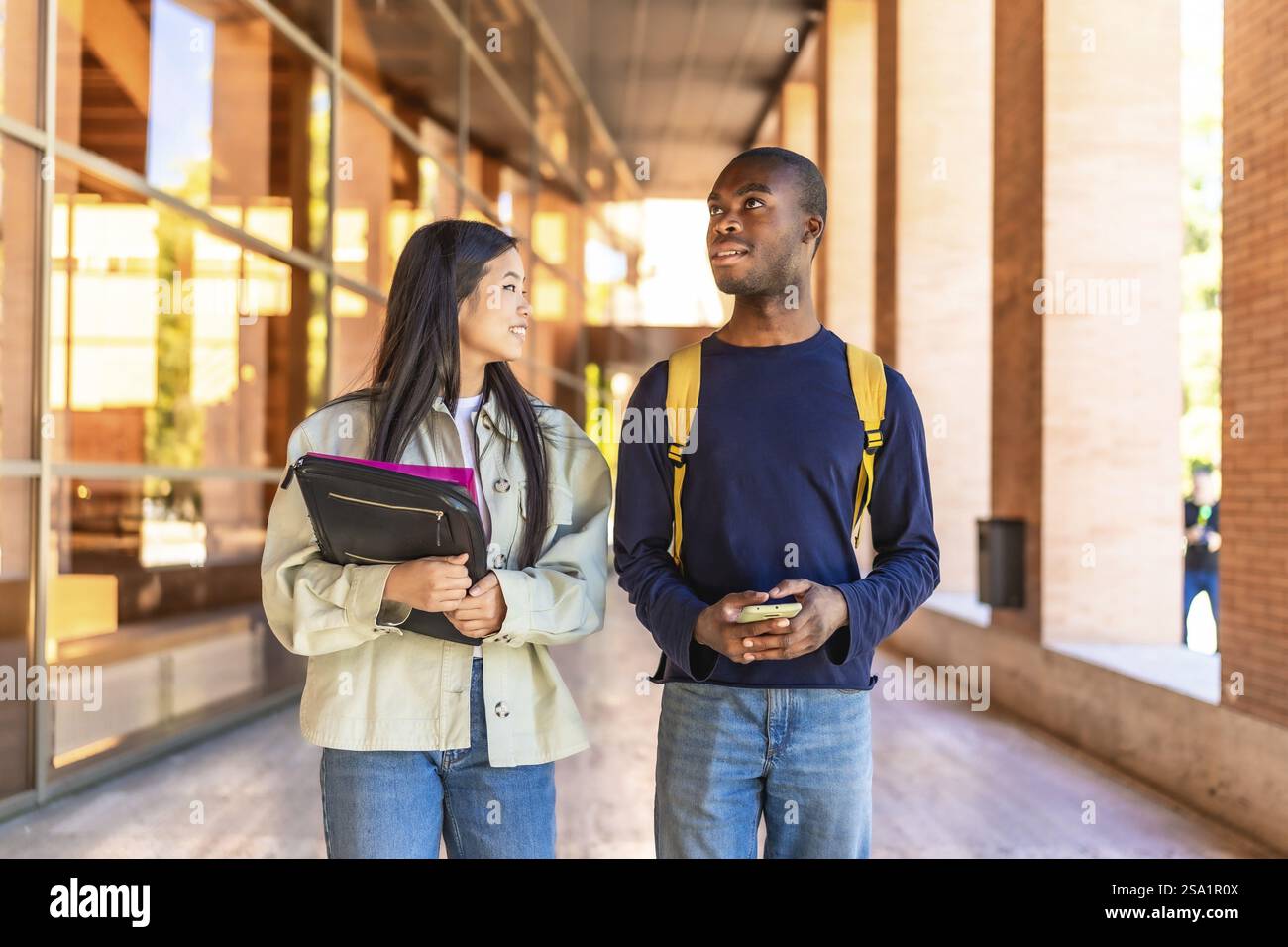 Two african and chinese multi-ethnic exchange students arriving at the university walking and ...