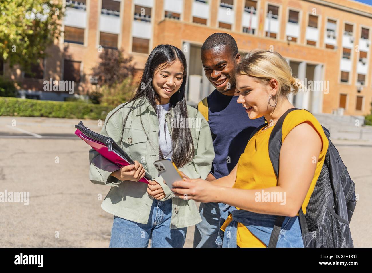 Three multi-ethnic students looking at the mobile phone together ...