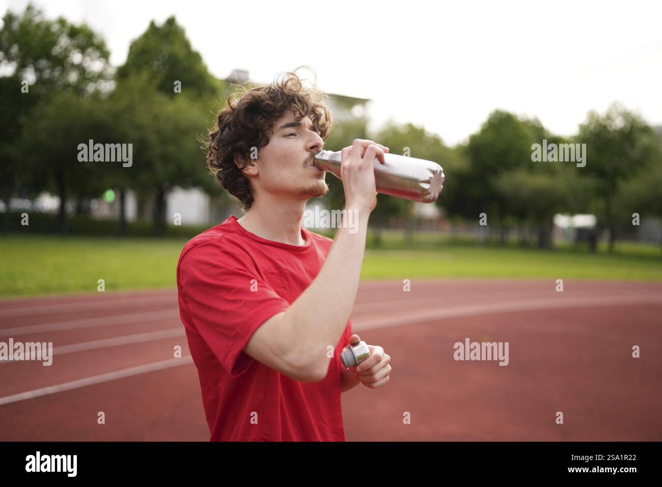Thirsty caucasian young amle athlete drinking water in a reusable ...