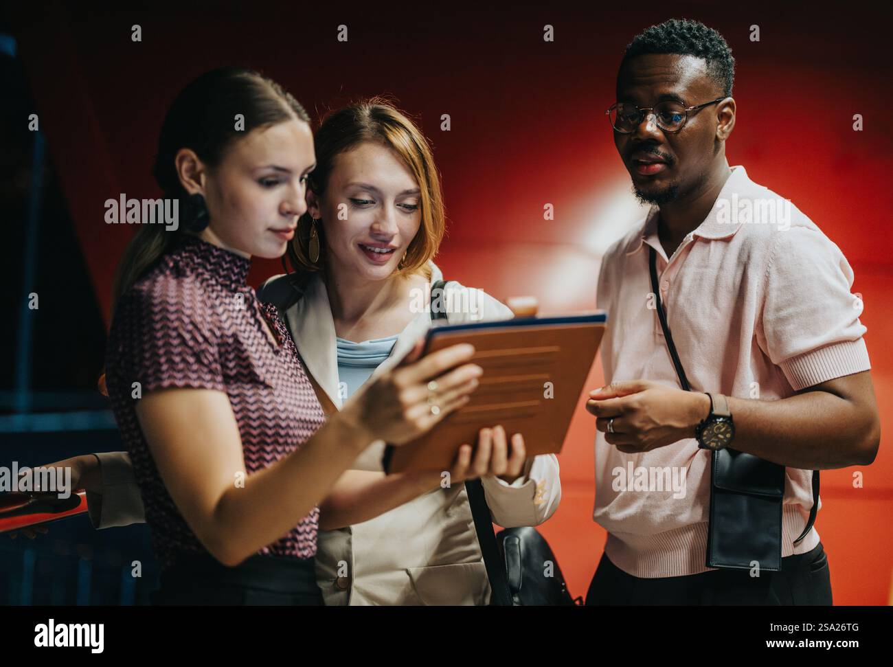 Three young people collaborating and discussing ideas while looking at a tablet in a modern ...