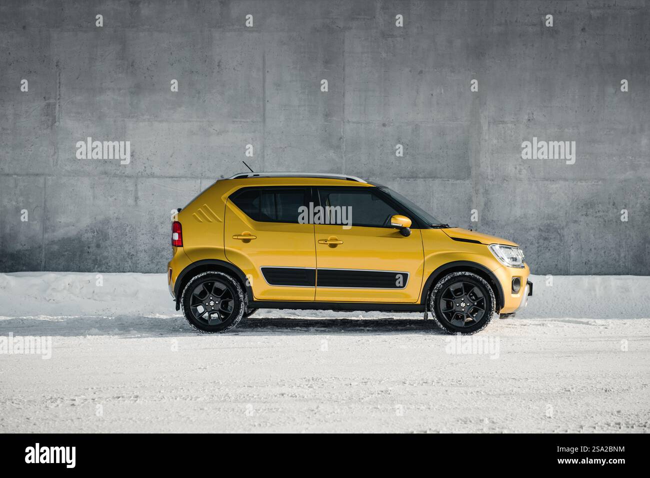 Golden Suzuki Ignis parked near concrete wall on a snow. Side view of ...