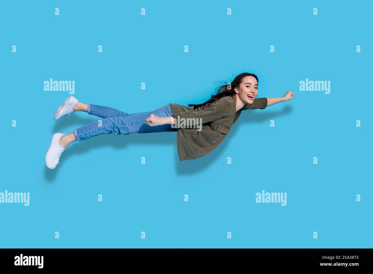 Happy young woman pretending to fly on vibrant blue background ...