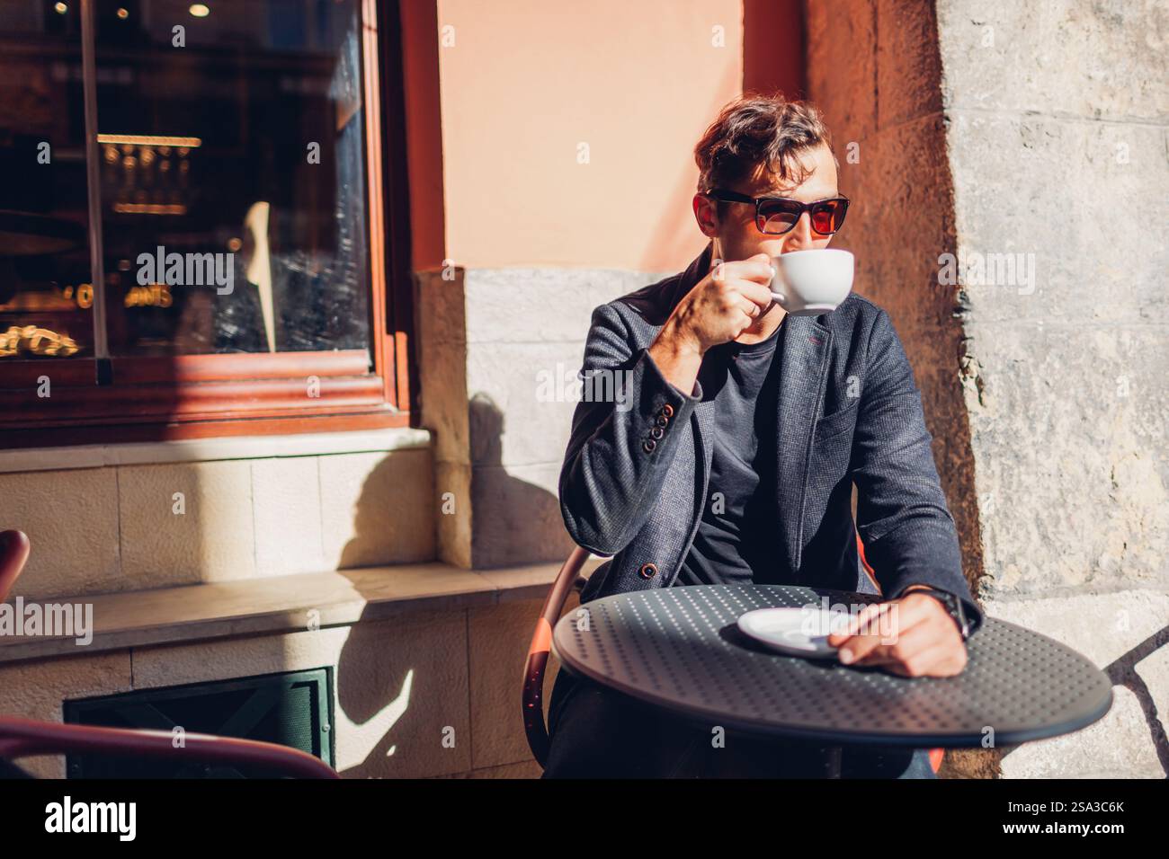 Young stylish man relaxes in cafe outdoor drinking coffee on terrace ...