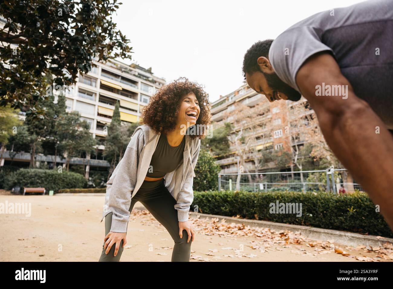 Two individuals happily engage in a fitness session in an outdoor city park setting, showcasing ...