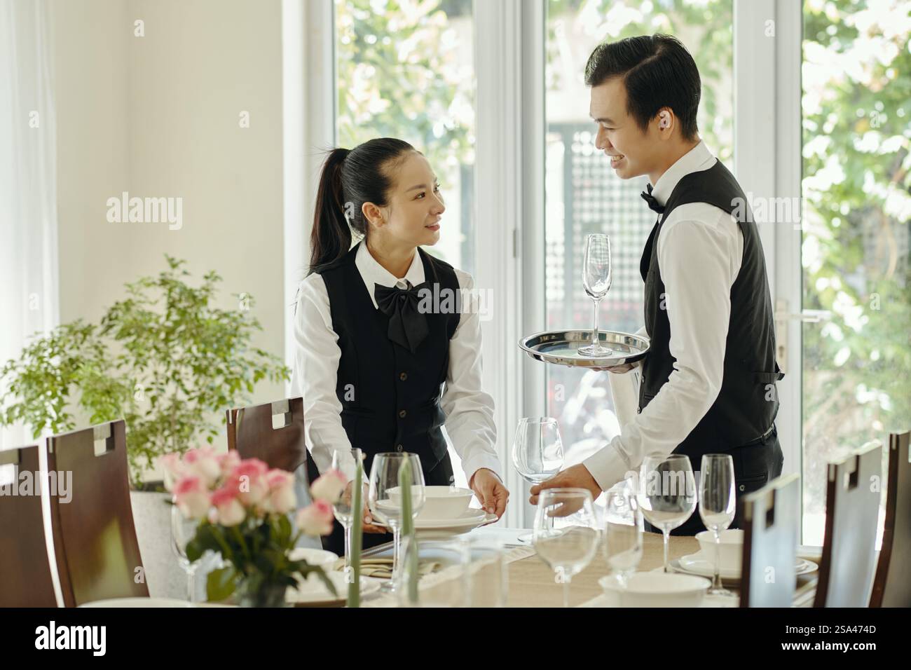 Professional waiters in uniform setting the dining table with plates ...