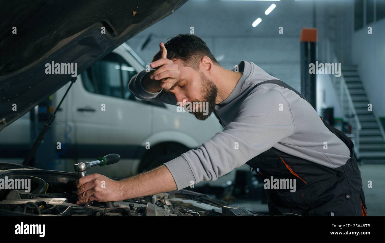 Caucasian mechanic in uniform repairing engine fixing motor inside open ...