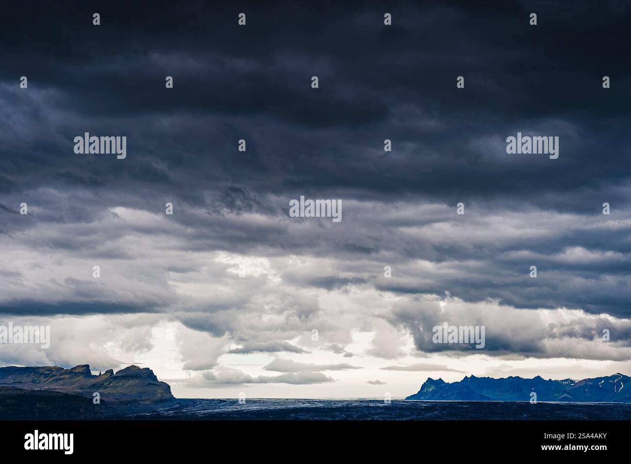 Dark clouds gather ominously above rugged mountain peaks in Iceland ...